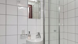 Casa de banho com lavatório branco, espelho e cabine de duche em vidro.