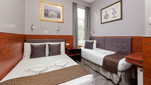 Quarto de hotel com duas camas, uma mesa de cabeceira, uma escrivaninha e uma janela com cortinas.