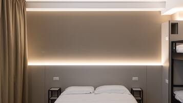 Quarto de hotel moderno com cama, mesas de cabeceira, prateleira embutida e uma janela grande com cortinas.