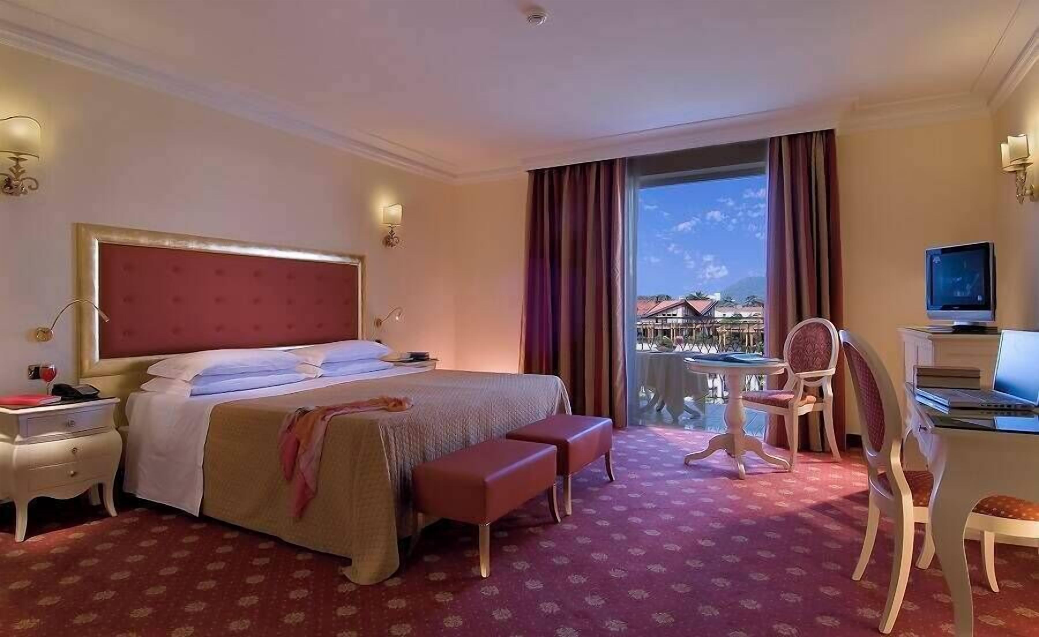 Quarto de hotel com uma cama grande, uma mesa com cadeira, televisão e varanda com vista.