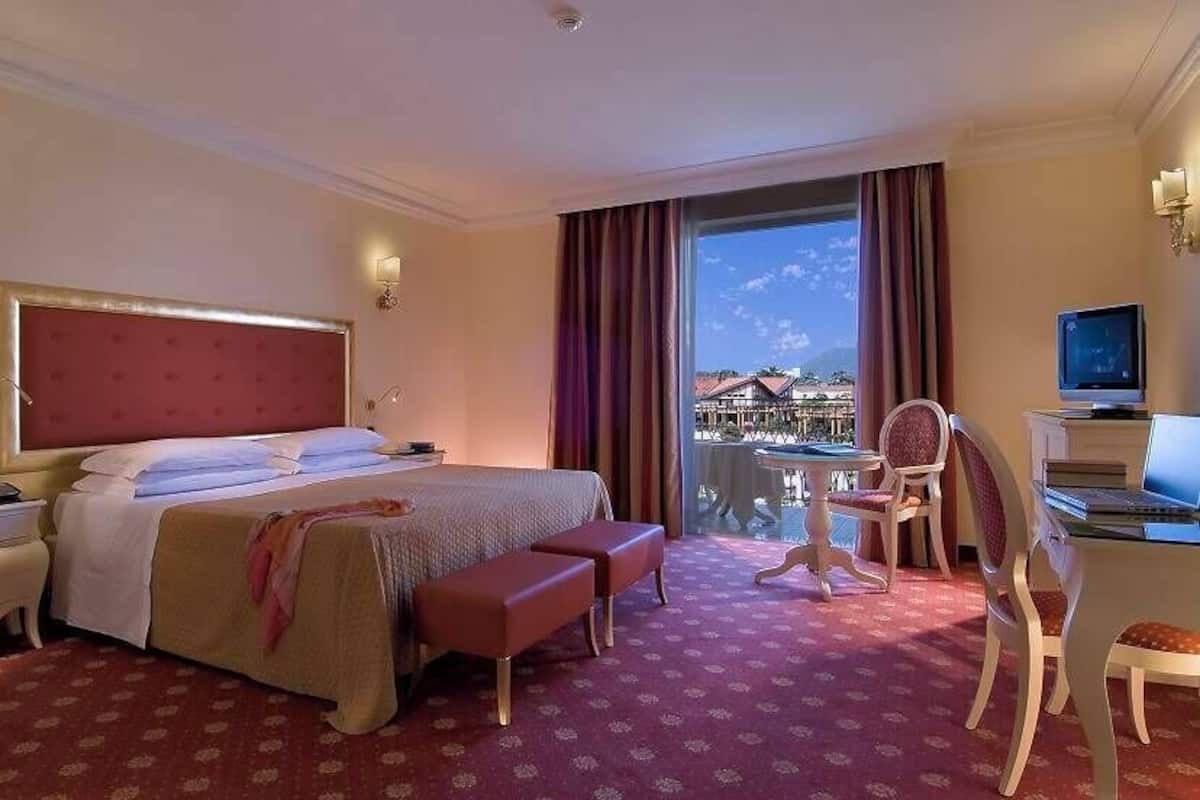 Quarto de hotel com uma cama grande, uma mesa com cadeira, televisão e varanda com vista.