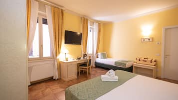 Quarto de hotel com cama, escrivaninha, cadeira, televisão e mala.
