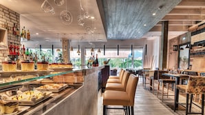 Uma área de bar moderna com um balcão comprido, banquetas e uma variedade de garrafas e copos nas prateleiras.