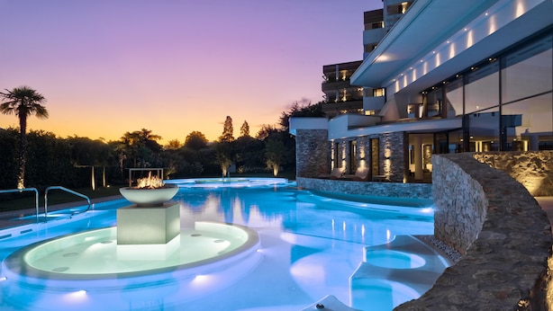 Um hotel moderno com uma grande piscina infinita, paredes de pedra e uma lareira.