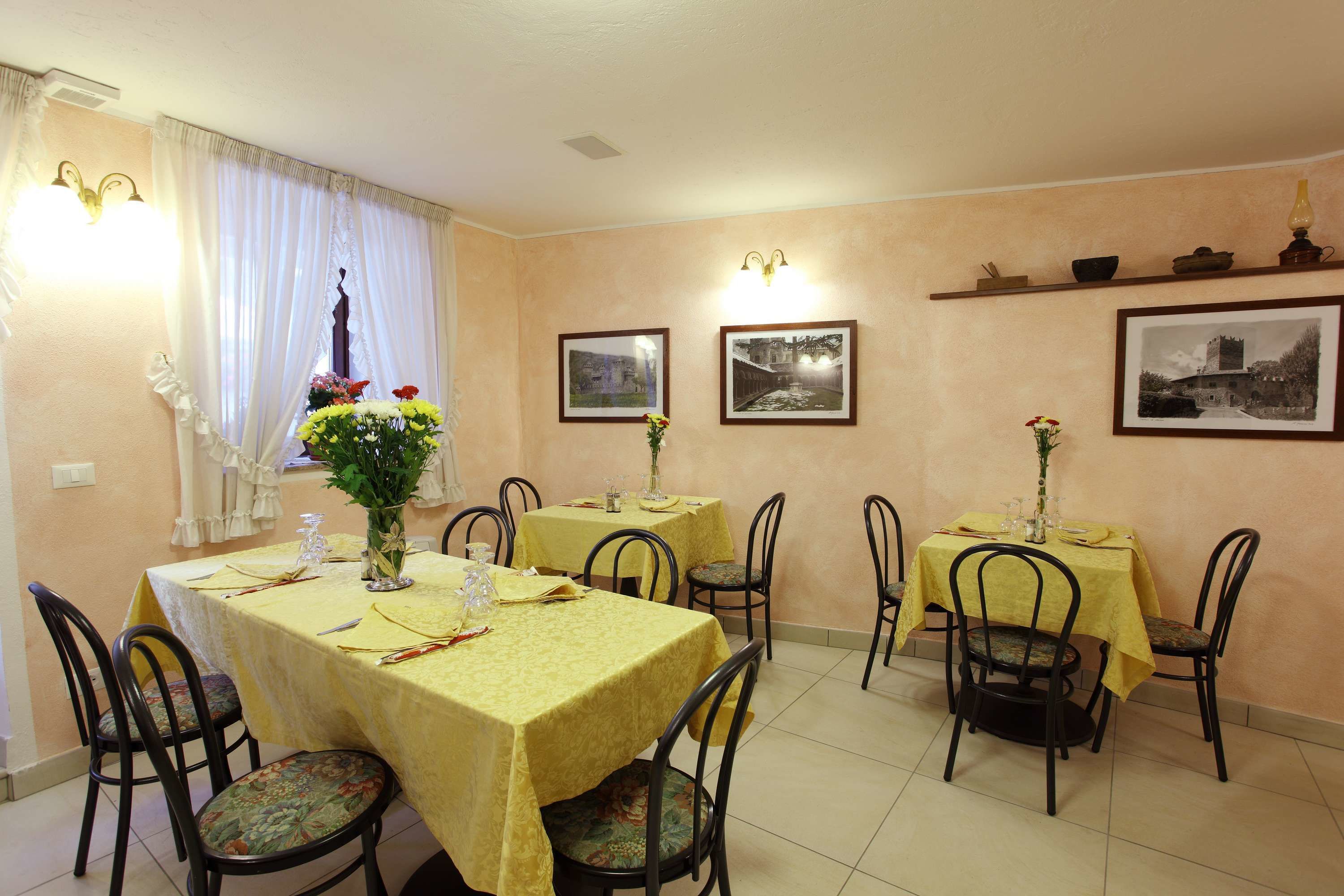 Uma sala de jantar com mesas preparadas para quatro pessoas, cada uma com toalha amarela, cadeiras e um vaso com flores.