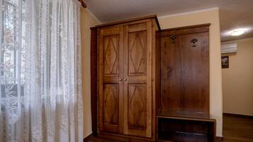 Quarto com guarda-roupa de madeira, uma mesinha e janela com cortina branca.