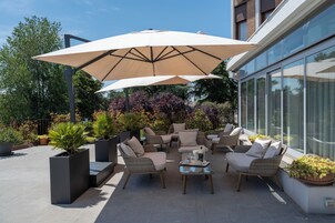 Área externa com mobiliário de vime, uma mesa central e grandes guarda-sóis para proteção do sol.