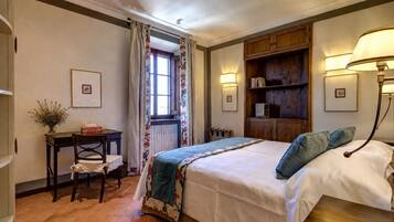 Um quarto com cama, abajures, uma estante de madeira, uma escrivaninha com cadeira e uma janela com cortinas.