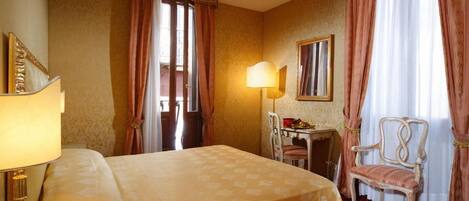 Quarto de hotel com cama, escrivaninha com luminária, cadeira, espelho e cortinas.