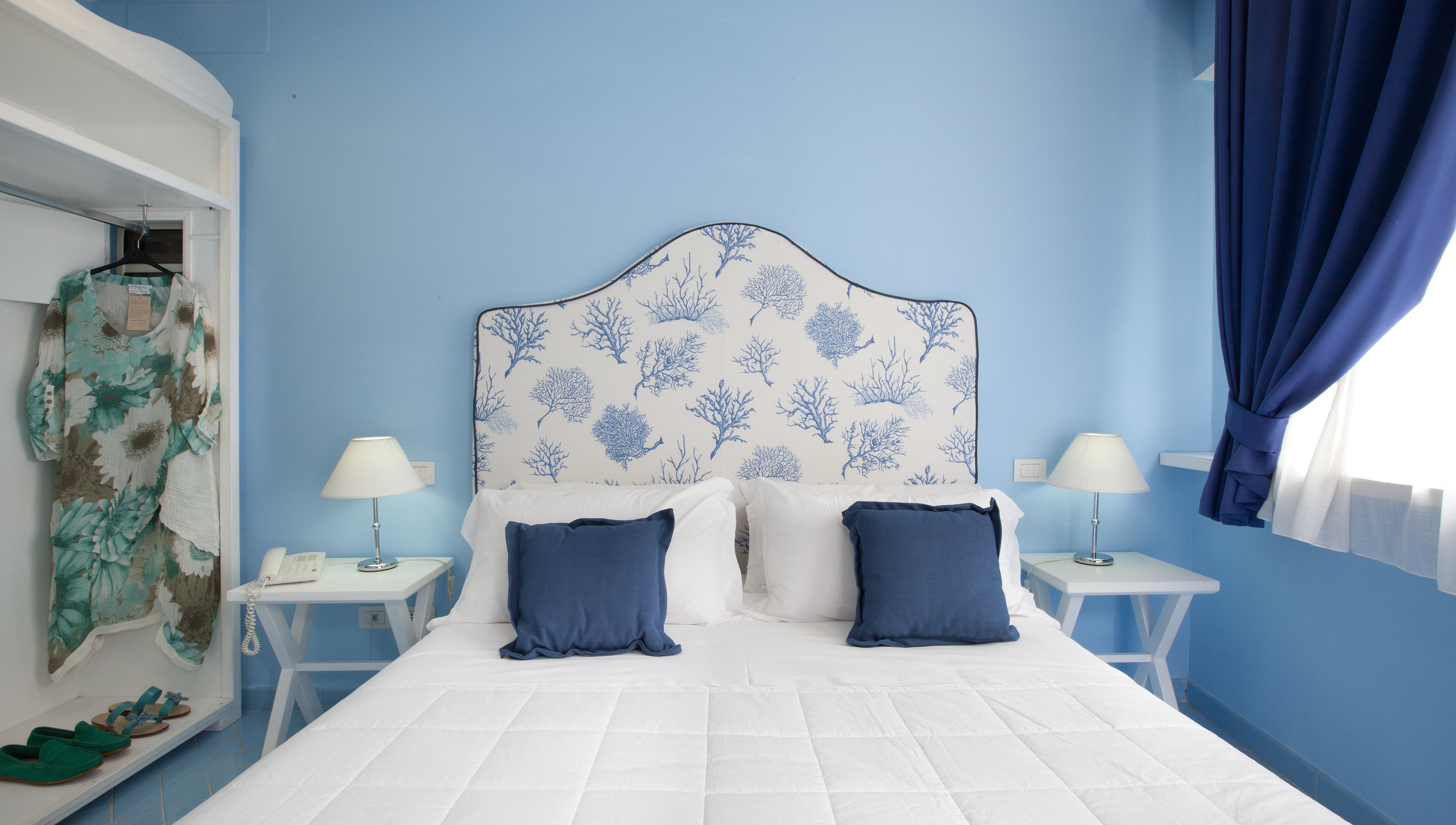 Quarto com cama, duas mesas de cabeceira, abajur, cabides e um par de chinelos.