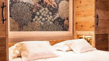 Quarto de cabana de madeira com cama, roupa de cama branca e uma grande pintura de veados e árvores na parede.