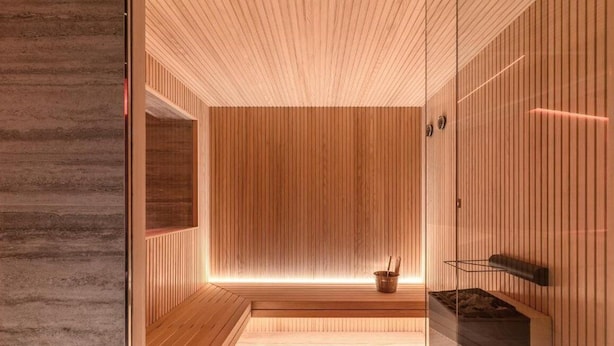 Uma sauna moderna com paredes de madeira, divisória de vidro e lareira integrada.