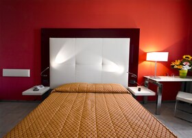 Quarto de hotel moderno com uma cama grande, mesa de cabeceira com abajur, telefone e um vaso com flores.
