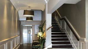 Um corredor amplo com piso de madeira escura, escada com corrimão escuro e uma grande luminária pendente preta.