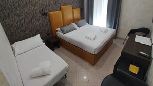Quarto de hotel com uma cama grande, uma cama menor, uma escrivaninha e uma cadeira.