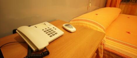 Quarto de hotel com mesa de cabeceira de madeira, telefone branco e mesinha de apoio.