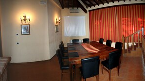 Sala de conferências com uma mesa comprida, cadeiras pretas, um pano de fundo vermelho e iluminação fixada na parede.