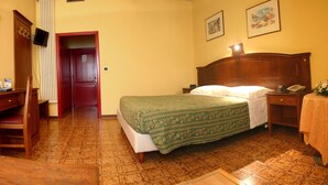 Quarto de hotel com cama, mesa de cabeceira e escrivaninha com cadeira.