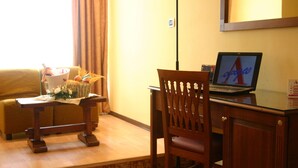Quarto com escrivaninha de madeira, um laptop, uma cadeira, um sofá e uma pequena mesa com uma tigela de frutas e flores.
