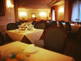 Uma área de refeições de hotel com várias mesas preparadas para hóspedes, com toalhas de mesa brancas e utensílios básicos.