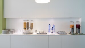 Disposição de buffet com recipientes de vidro transparente, dispensadores de água e um lustre pendente.