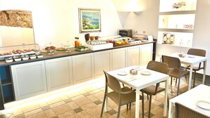 Um buffet de café da manhã com diversas opções de comida, uma pintura na parede e uma área de estar com mesas e cadeiras.