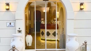 Entrada de hotel com porta de vidro, um vaso branco e uma barreira de corda.