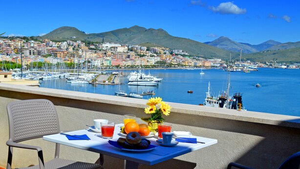 Uma mesa com itens de café da manhã e vista para uma marina com barcos e um horizonte urbano ao fundo.