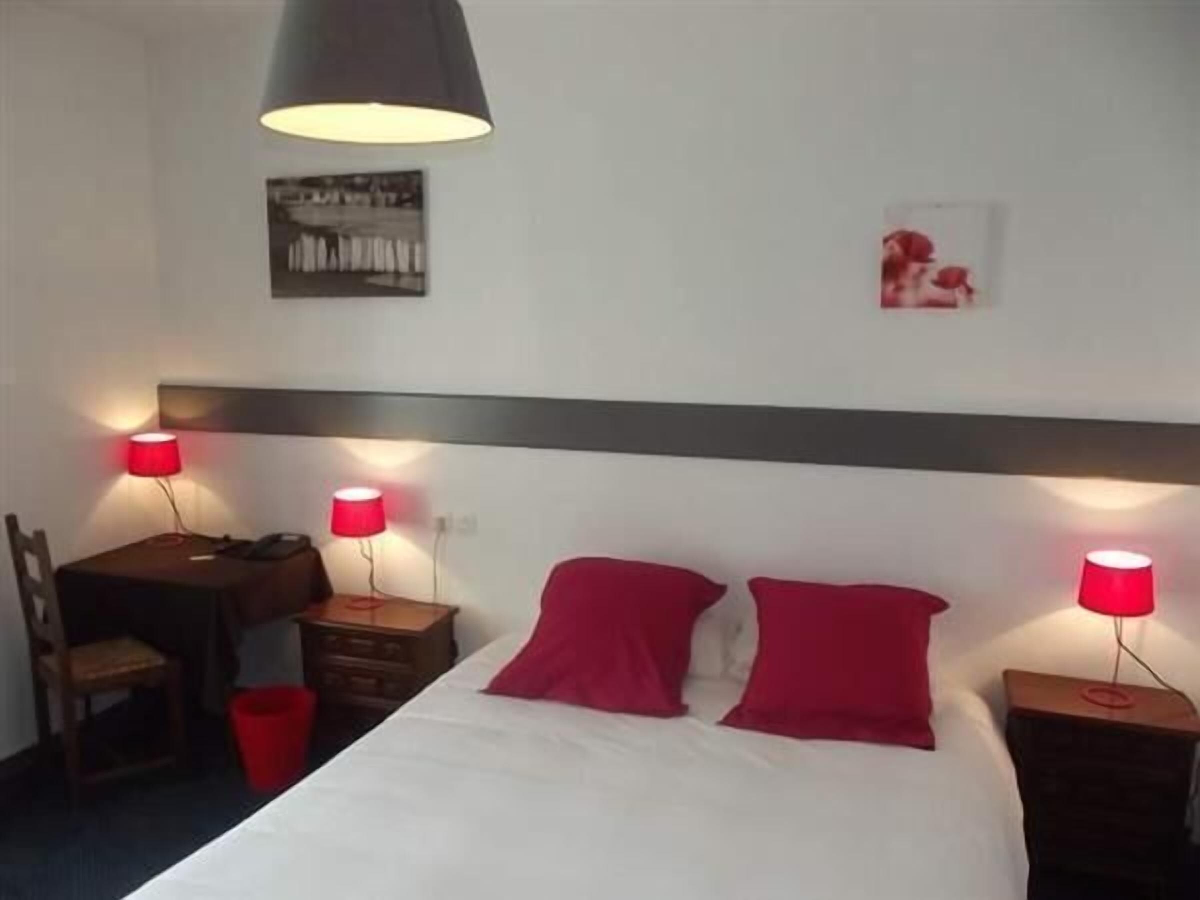 Quarto de hotel com uma cama, duas mesas de cabeceira com luminárias, uma escrivaninha com cadeira e uma luminária na parede.