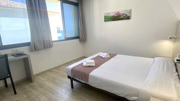 Quarto de hotel com cama, escrivaninha e janela com cortinas.