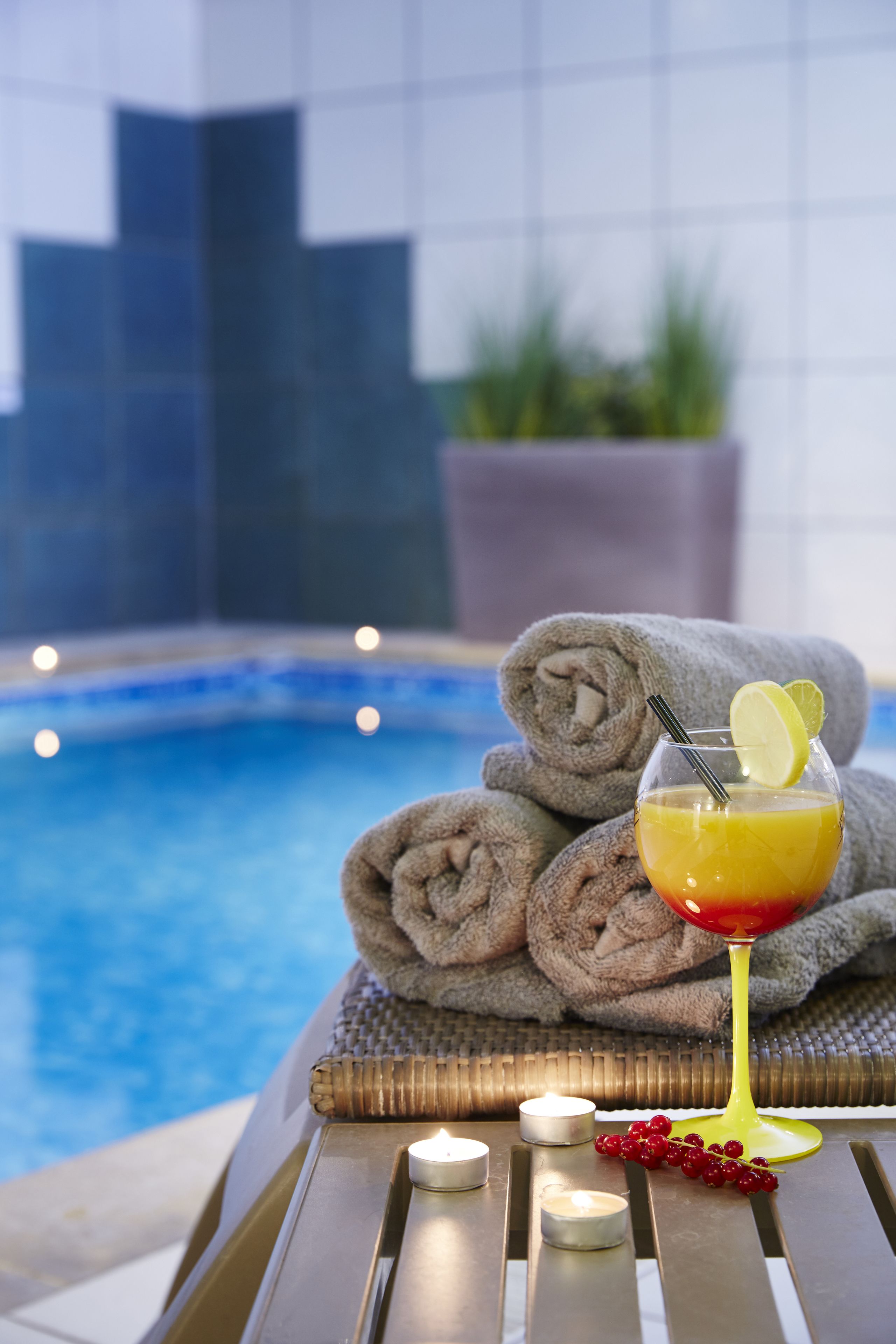 Cenário à beira da piscina com um copo de sumo de laranja, uma toalha e velas.