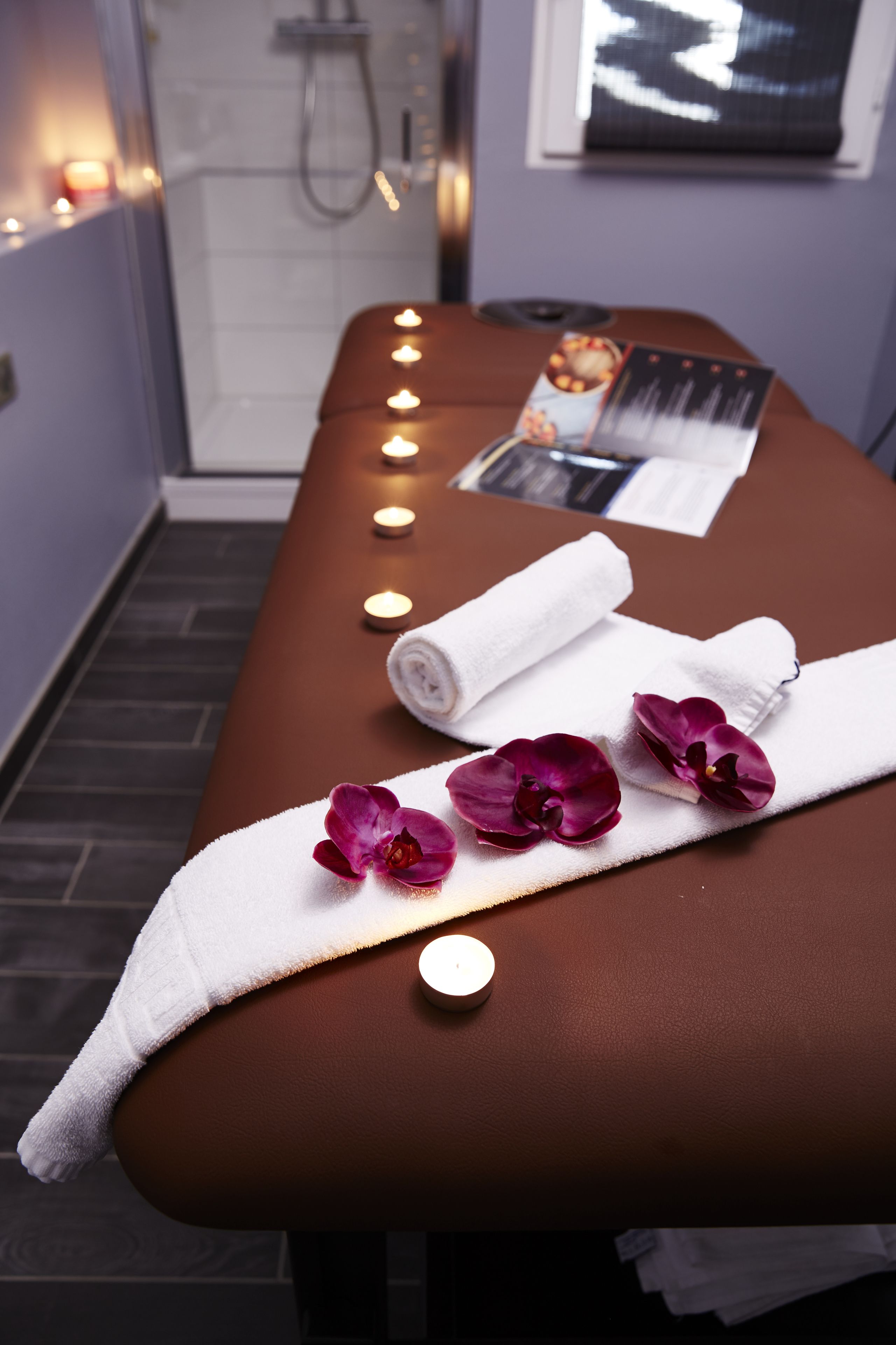 Uma mesa de massagem com velas, toalhas e flores.