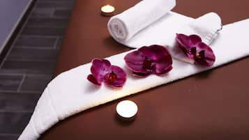 Uma mesa de massagem com velas, toalhas e flores.