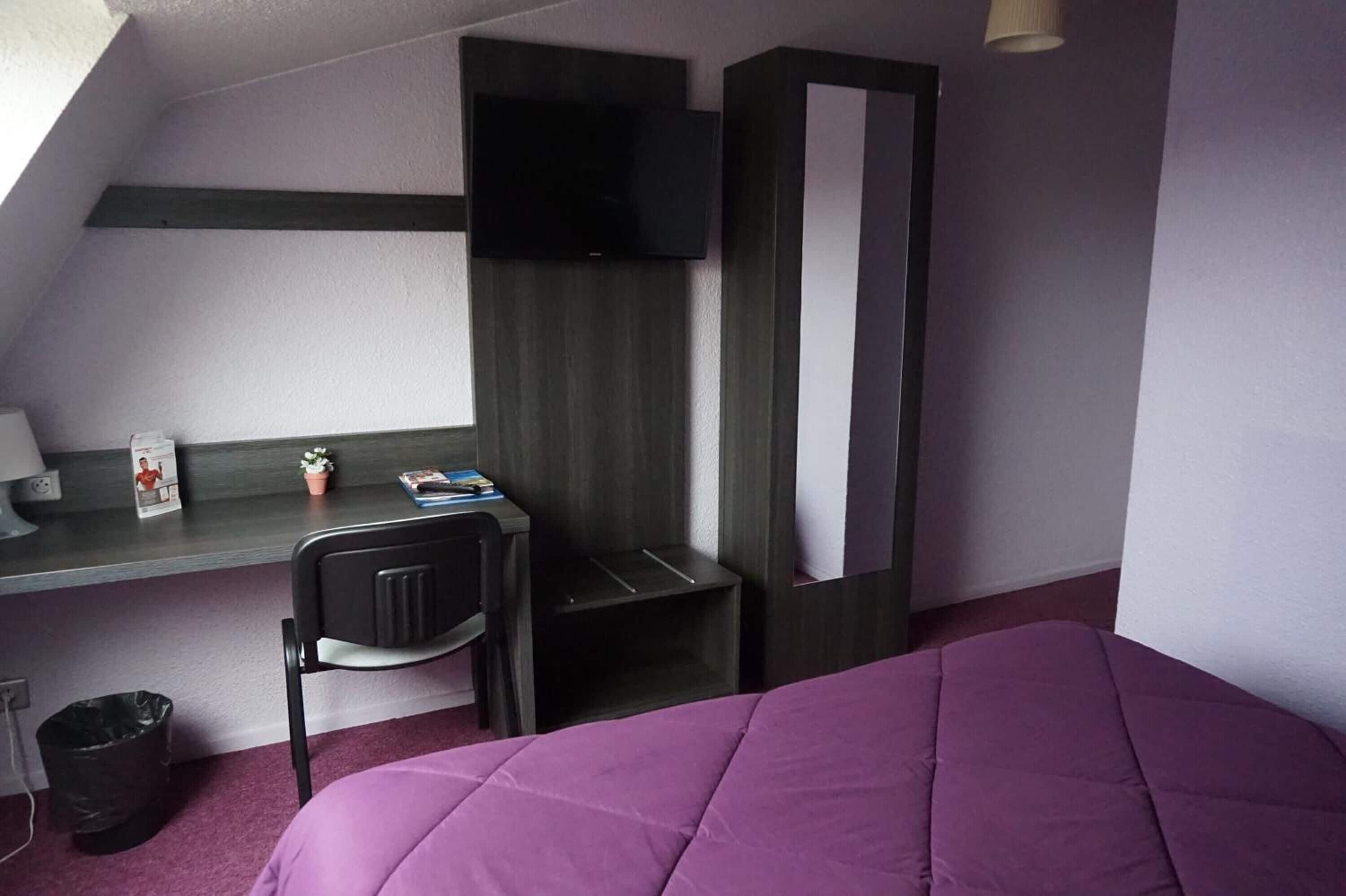 Quarto com cama, escrivaninha, cadeira, televisão e um pequeno armário.