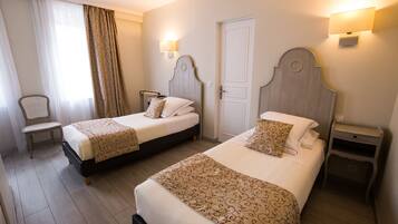 Quarto de hotel com duas camas, uma cadeira, uma mesa de cabeceira e uma porta.