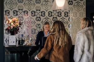 Uma área de bar com parede estampada, balcão com um vaso de flores e uma pessoa parada no balcão.