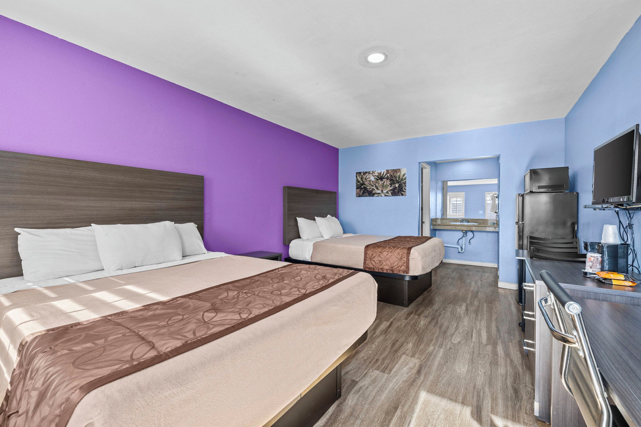 Quarto de hotel com duas camas, televisão, frigorífico e uma pequena cozinha equipada.