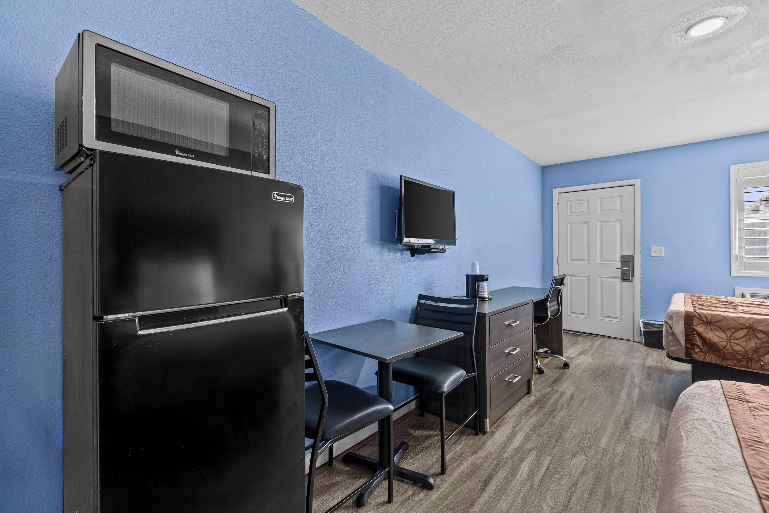 Quarto compacto com cozinha compacta, uma cama, escrivaninha com cadeira e televisão.