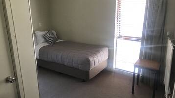 Quarto com cama, uma mesinha e janela com persianas.