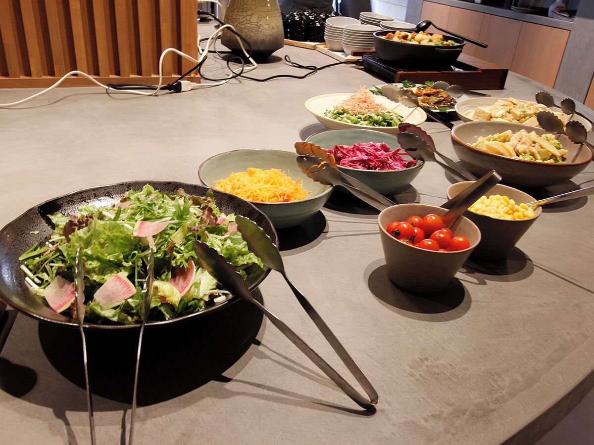 Mesa de buffet com diversos pratos, incluindo salada, queijo e uma tigela de tomates cereja.