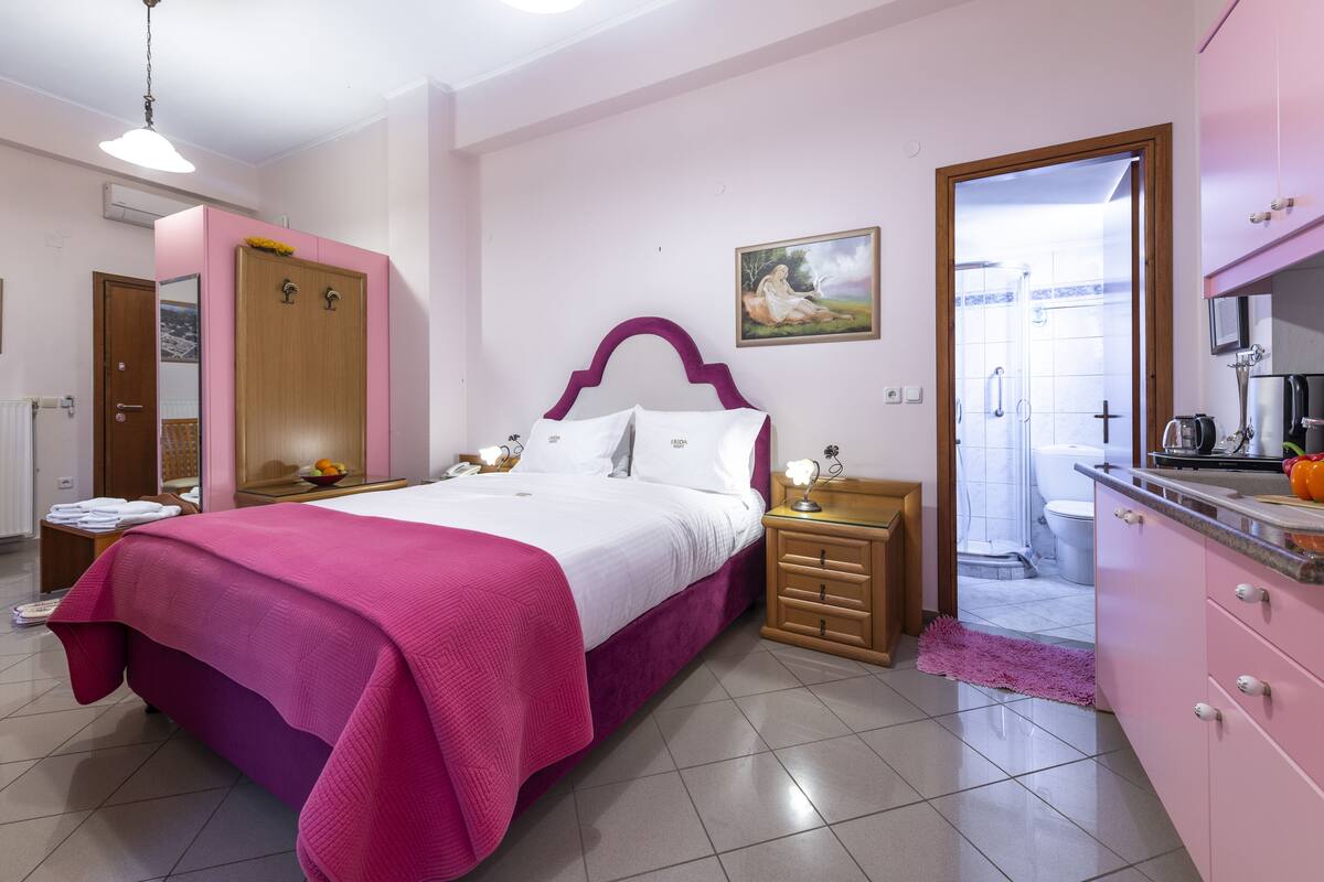 Quarto com cama, mesas de cabeceira, guarda-roupa e banheiro visível por uma porta aberta.