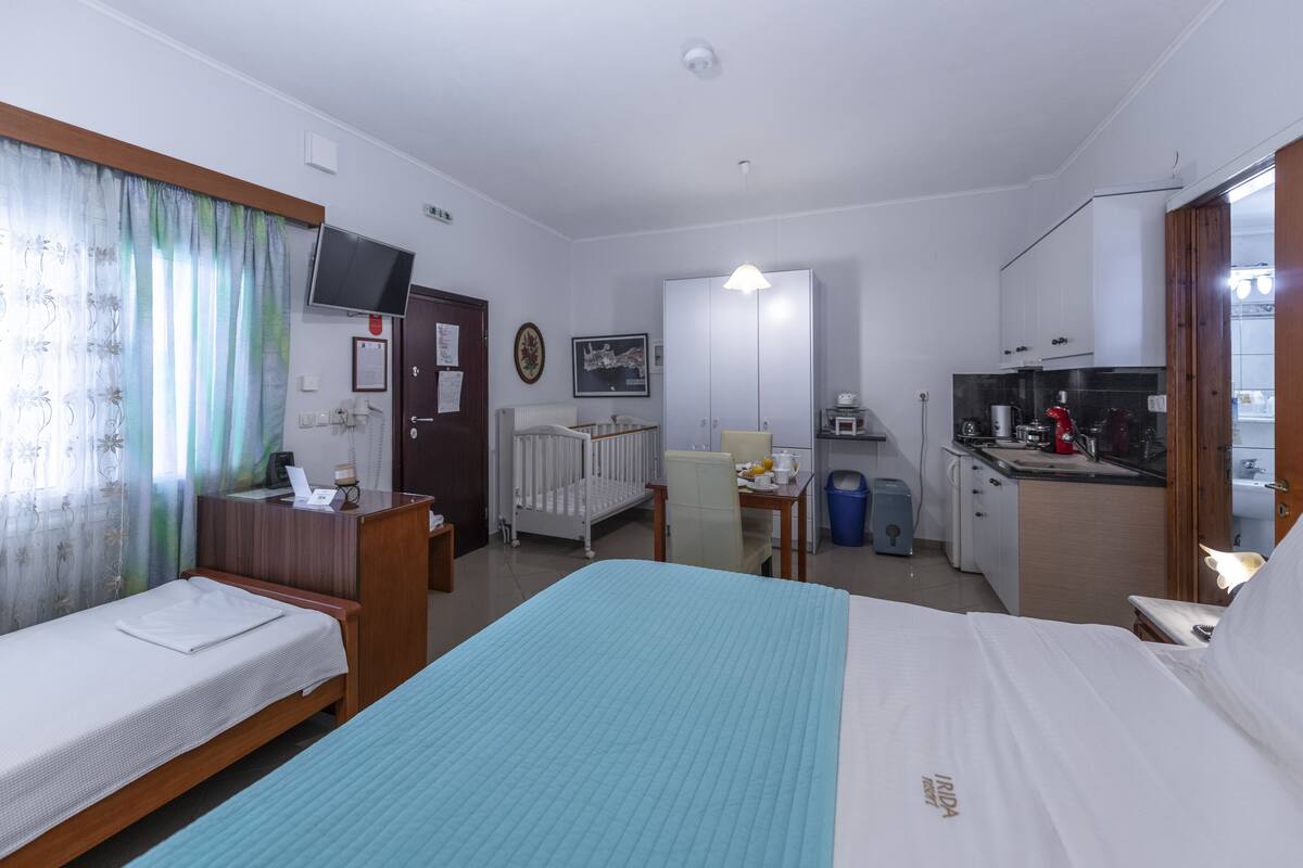 Quarto de hotel com uma cama de solteiro, escrivaninha, cadeira, pequena cozinha e berço, além de uma televisão.