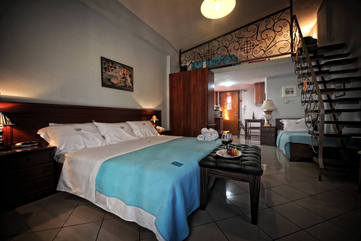 Quarto de hotel com cama, escrivaninha, cadeira, escada e banheiro.