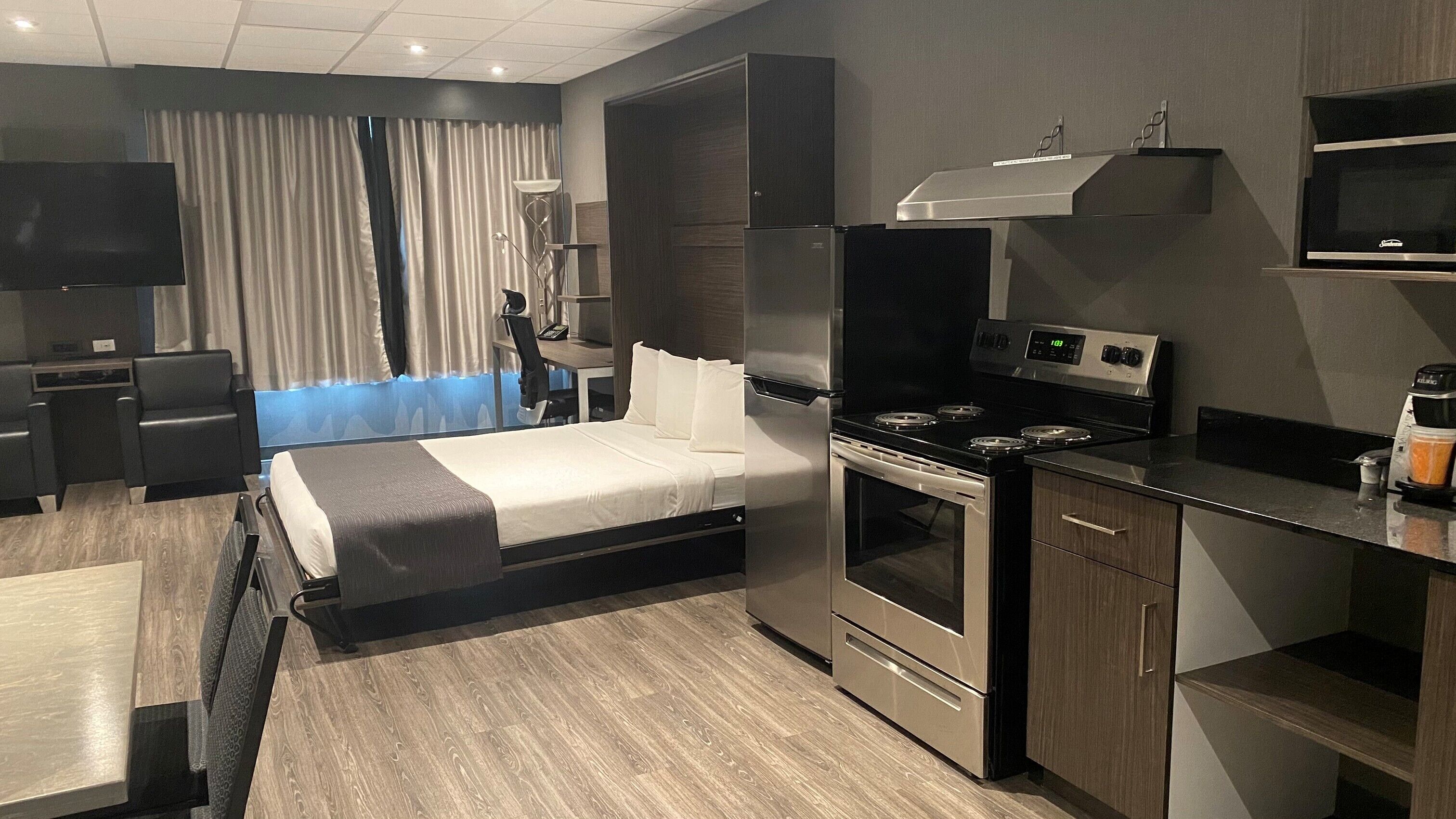 Quarto de hotel moderno com cama, escrivaninha, televisão, micro-ondas e fogão.
