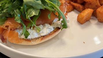 Sanduíche com folhas, salmão defumado e molho cremoso, acompanhado de batatas assadas e uma fatia de melancia.