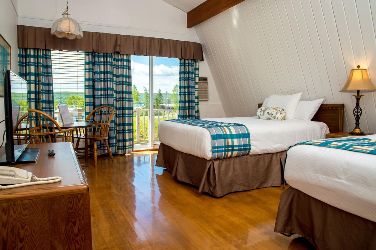 Quarto de hotel com duas camas, uma mesa com telefone, uma cadeira e vista para o exterior.