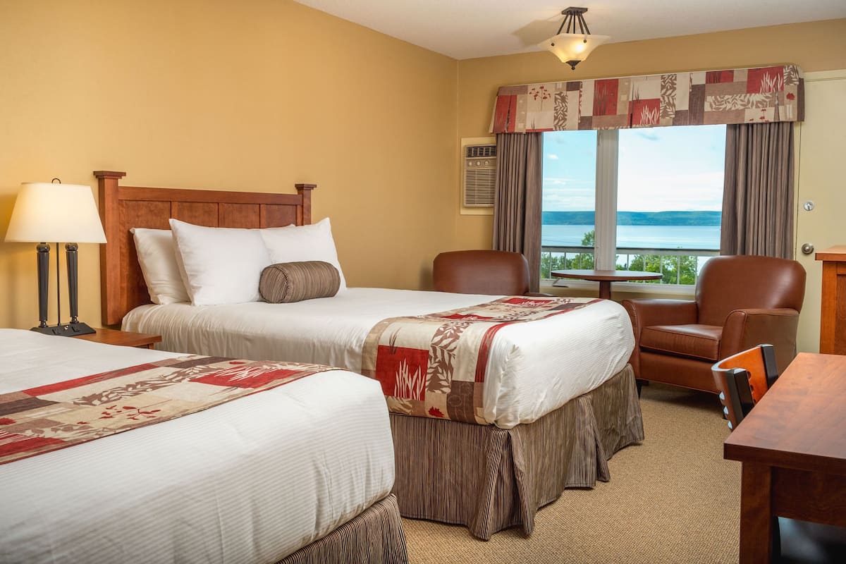Quarto de hotel com duas camas, uma cadeira, uma mesa e vista para o exterior.