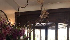 Um hall com um grande arranjo de flores, porta de entrada de vidro e um lustre.