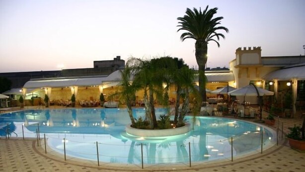 Piscina com uma palmeira ao centro, rodeada por espreguiçadeiras e guarda-sóis.