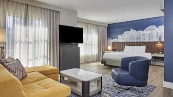 Quarto de hotel com cama, sofá, televisão e um mural com vista para a cidade.